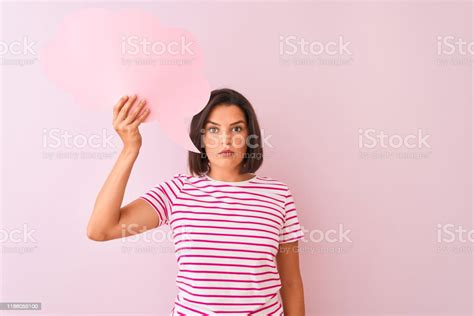 젊은 아름다운 여자는 심각한 생각 스마트 얼굴에 자신감 표정으로 고립 된 분홍색 배경 위에 서 구름 연설 거품을 들고 갈색 머리에 대한 스톡 사진 및 기타 이미지 Istock