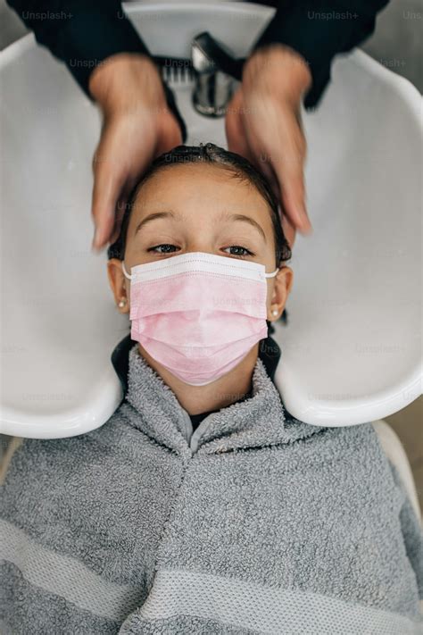 전문 미용사가 부드럽게 머리를 씻는 동안 헤어스타일 치료에서 보호용 얼굴 마스크를 쓴 어린 소녀 코로나 바이러스 라이프 스타일과 새로운 정상 개념 사진