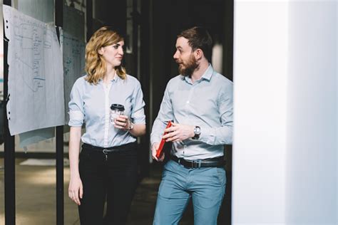 손에 노트북을 들고 젊은 남자가 손에 가서 홍보 영역 근처 복도를 따라 가서 커피를 들고 여성 동료와 이야기 근무 일정을 논의하는 놀란 남성 직원 경영자에 대한 스톡 사진