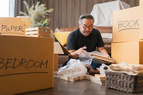 성인 아시아 남자 남성 흰 수염은 상자에 물건을 포장하고 거실 가정 이동 아이디어 개념에 그들을 테이핑하는 새로운 집으로 이동을 준비하기 위해 바닥에 앉아 짐 싸기에 대한