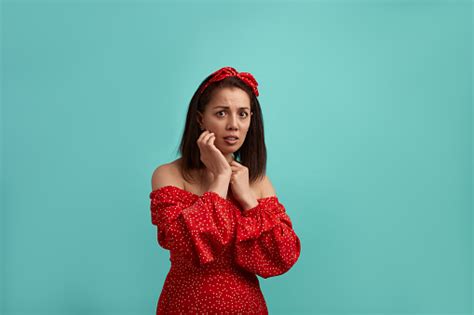 무서운 충격 유럽 여성 머리 밴드를 착용 맨 어깨와 빨간 드레스에 갈색 머리는 나쁜 행동의 결과에 의해 두려워 뺨을 터치 청록색 배경에 고립 된 조심스럽게 보인다 30 39