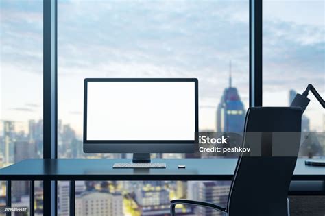 책상 위에 빈 흰색 컴퓨터 모니터가 있고 아름다운 도시 전망과 일광이 있는 탁 트인 창문이 있는 현대적인 사무실 인테리어 모형
