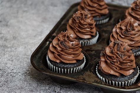 수제 초콜릿 컵케이크가 들어있는 머핀 케이크 주석의 이미지 초콜릿 버터 아이싱 파이프 소용돌이 초콜릿 조각 회색 배경 높은 전망 전경에 초점 복사 공간 컵케이크에 대한 스톡