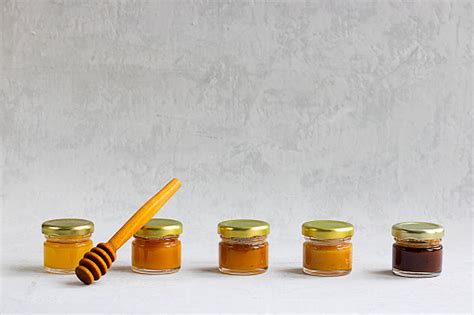 다른 종류와 꿀의 색상과 금속 캡 다섯 작은 유리 항아리 라인과 나무 숟가락 분리 및 복사 공간 회색 시멘트 배경에 넣어 건강 한 제품 자연 수평 0명에 대한 스톡 사진 및