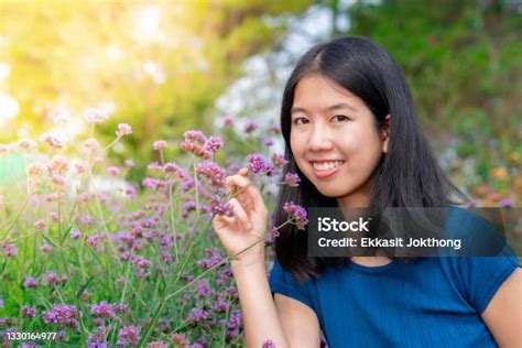 ภาพของหญิงชาวเอเชียผมยาวสวยในเสื้อเชิ้ตสีน้ําเงินมองดอกไม้สีม่วงในสวนอย่างมีความสุขด้ ภาพสต็อก