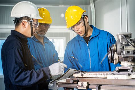 밀링 머신에서 일하는 아시아 기계 노동자 안전 예방 조치를 위해 기계를 작동 할 때 보호 안경과 헬멧을 착용한 기술자 리더는 팀원에게 일을 하라고 조언합니다 교습에 대한