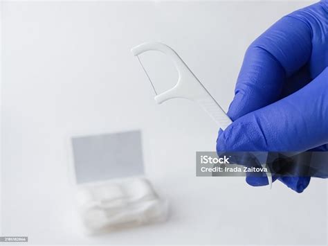 파란색 의료용 장갑을 낀 치과 의사의 손은 치실을 클로즈업하고 치실 패키지를 배경으로 들고 있습니다 치아 청소에 대한 치과 의사의 권장 사항 간호사에 대한 스톡 사진 및