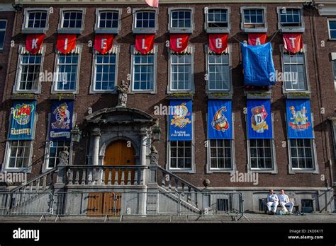 Two Men Are Sitting On A Bank Close To A Facade Decorated With The