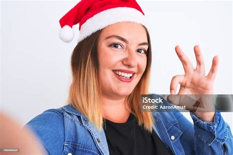 크리스마스 산타 모자를 입고 아름다운 여자는 손가락 우수한 기호와 확인 기호를하고 고립 된 흰색 배경을 통해 셀카를 확인 12월에 대한 스톡 사진 및 기타 이미지 Istock