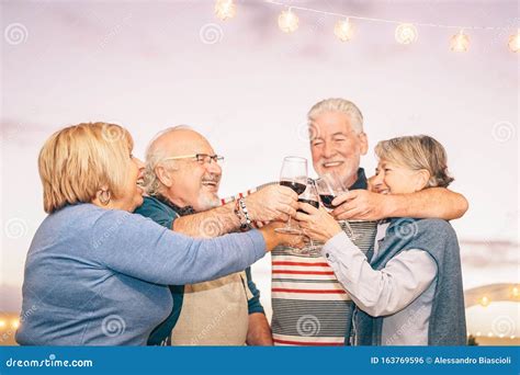 Happy Senior Friends Cheering And Toasting With Red Wine On Terrace