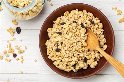 건강한 아침 식사 흰 나무 테이블에 점토 그릇에 말린 포도를 곁들인 뮤즐리 뮤즐리는 테이블에 흩어져 있습니다 텍스트 공간입니다 아침식사 시리얼에 대한 스톡 사진 및 기타