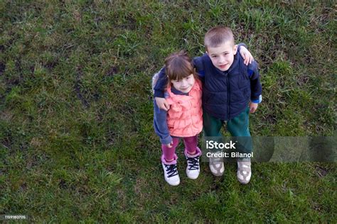 녹색 잔디에 서있는 캐주얼 한 옷을 입은 두 명의 귀여운 아이들의 위에서 보면 어깨 위로 서로 껴안고 수줍은 미소를 지으며