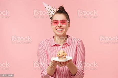 유색 안경과 생일 모자를 쓴 흥분된 재미있는 십대 소녀 두 손으로 접시에 케이크를 들고 눈을 감고 분홍색 배경에 고립 된 소원을 합니다 여자에 대한 스톡 사진 및 기타