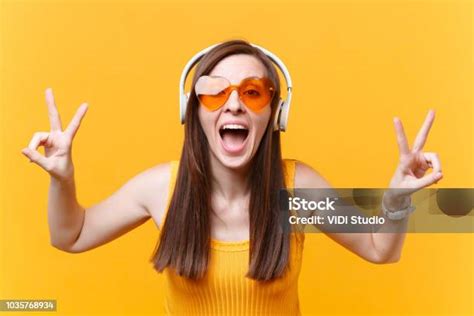흥분된 재미의 오렌지에서 소녀 안경 승리 손가락 기호 노란 배경에 고립 된 복사 공간을 보여주는 헤드폰에서 듣는 음악 사람들이 진심으 감정 개념 광고 영역입니다 가리키기에