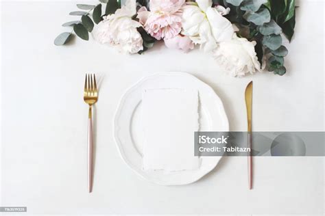 여성 결혼식 생일 바탕 화면 모형 장면입니다 도자기 접시 빈 면 종이 인사말 카드 황금 칼붙이 유칼립투스와 모란 꽃 흰색 테이블 배경입니다 플랫 레이 상단 보기 결혼식에