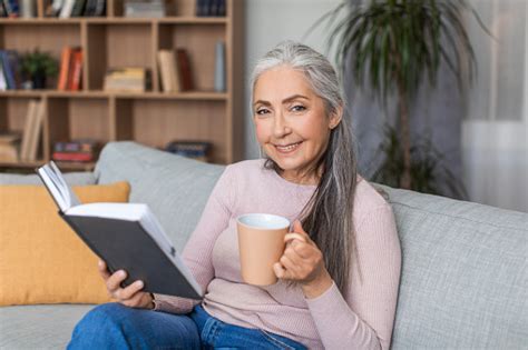 회색 머리를 가진 쾌활한 유럽 노인 여성은 커피를 마시고 여가 시간에 좋아하는 책을 읽습니다 60 64세에 대한 스톡 사진 및 기타 이미지 Istock