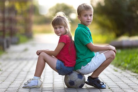 두 귀여운 금발 행복 한 어린 아이 미소 소년과 긴 머리 소녀 빈 햇볕이 잘 드는 교외 포장 도로에 축구 공에 백투백 앉아 여름 밝은 배경을 흐리게 어린이 게임 개념입니다