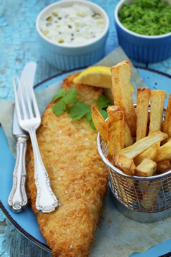 기름진 양피지 칼과 포크 레몬 슬라이스 타르타르 소스와 무시 완두콩을 함유 한 그릇 청록색 나무 곡물 배경 높은 전망과 청록색 접시에 파슬리로 장식 된 피시 앤 칩스 의