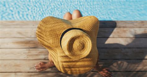 야자수 아래 나무 부두에서 휴식을 취하는 모자를 쓴 아름다운 여자는 수영장 가장자리에 그림자를 남기고 여름 휴가를 즐기고 있습니다 수영장에서 일광욕을 하는 날씬한 젊은