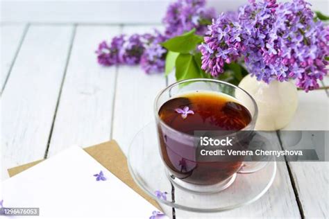 라일락 꽃 투명한 차 한 잔 접시 흰색 꽃병 흰색 및 공예 노트 종이흰색 나무 판이 있는 섬세한 아침 차 테이블 세팅 Mockup 공간을 복사합니다 봄 아침 식사 컨셉 0