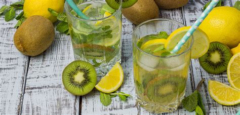 여름에는 빨 대가 있는 유리잔에 상쾌한 음료 회색 나무 테이블에 레몬 키 위 민트와 얼음 조각과 차가운 달 콤 하 고 새 콤 한