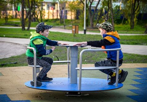 Brightly Dressed Twin Brothers Play On A Carousel In An Autumn Park Amid Fallen Yellow Leaves