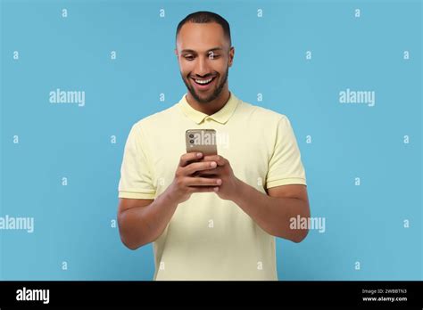 Happy Man Sending Message Via Smartphone On Light Blue Background Stock