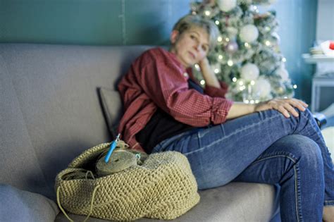 성탄절을 위해 장식된 거실의 소파에 누워 있는 금발의 여인 크로 셰 뜨개질 취미 로 포장 된 크로 셰 뜨개질로 묶인 Jute 가방은 전경의 소파에 놓여 있습니다 바구니에