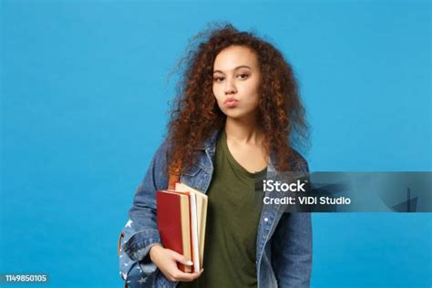 데님 옷에 젊은 아프리카계 미국인 소녀 사춘기 학생 배낭은 파란색 벽 배경 스튜디오 초상화에 고립 된 책을 잡아 고등학교 대학 대학 개념에서 교육 복사 공간을 모의 가방에