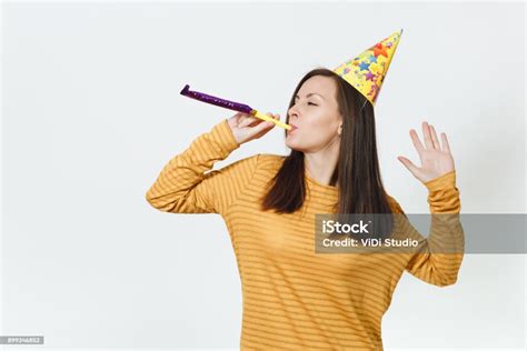 아름 다운 백인 재미 재생 파이프 축 하 광고에 대 한 격리 하는 흰색 바탕에 휴가 즐기는 노란색 옷에 생일 파티 모자 갈색 긴 머리를 가진 젊은 행복 한 여자 사람들에