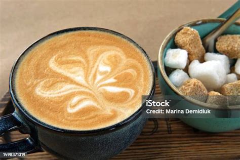 나무 카페 테이블에 꽃 모양의 거품이 있는 뜨거운 카푸치노의 파란색 세라믹 컵 아름다운 라떼 아트 거품 트렌디 한 정통 현대 도자기 세트 도자기 수제 커피 머그잔은 설탕