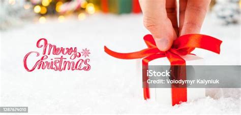메리 크리스마스 인사말 카드는 눈 위에 빨간 리본이 달린 선물 상자를 들고 있는 남자 손으로 배경에 흐린 불빛을 들고 있었다