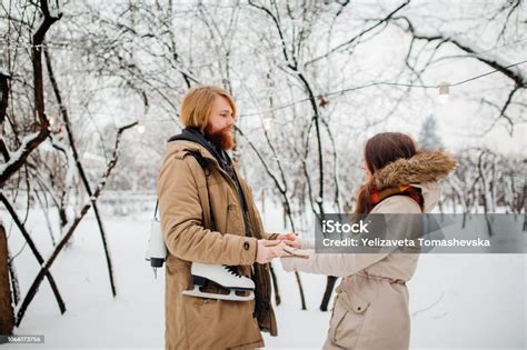 겨울 그리고 날짜입니다 젊은 부부 연인 남자와 눈과 손을 잡고 웃 고 숲의 배경에서 겨울에 여자 긴 머리와 수염 사람이 스케이트 들고 고 여자 보고 2명에 대한 스톡 사진
