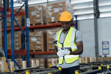 유통 창고 다민족 노동자 제품 바코드 스캐너 아프리카계 미국인 남성 창고 작업자는 안전 유니폼 헬멧을 착용하고 보관 창고에서 제품 품질을 검사합니다 25 29세에 대한 스톡