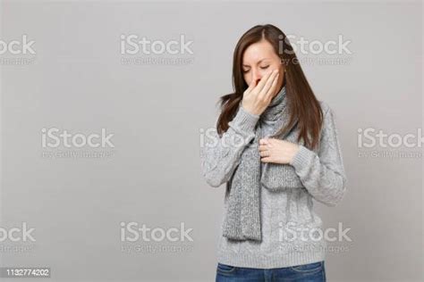 회색 스웨터 스카프에 젊은 여자 재채기 또는 회색 벽 배경에 고립 된 손바닥으로 입을 덮고 기침 건강 한 라이프 스타일 아픈 질병 치료 추운 계절 개념입니다 복사 공간을