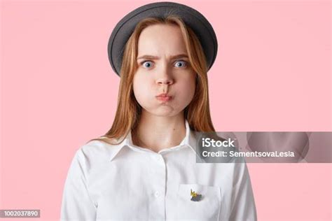 화가 블루의 즐거운 모습으로 여성을 눈 뺨을 불면 우아한 검은 모자와 흰색 셔츠를 착용 심 술 식 분홍색 배경 포즈가 얼굴 표정 개념 볼에 대한 스톡 사진 및 기타 이미지