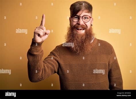 Handsome Irish Redhead Man With Beard Wearing Glasses And Winter Sweater Over Yellow Background