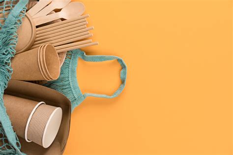 친환경 종이 기구 복사 공간이있는 오렌지 배경에 면 그물 가방에 크래프트 종이 식품 컵과 용기 모형 컵 접시 음주 빨대 나무 칼붙이 길거리 음식은 종이 식기를 빼앗습니다