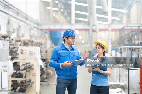플라스틱 공장에 있는 미국인 남성과 아시아인 엔지니어 두 명의 사진 함께 일하고 대화하고 목록 노트에서 문서를 확인하는 기계가 있습니다 유니폼과 헬멧을 착용하십시오 25