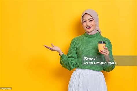 종이 커피 컵을 들고 녹색 스웨터에 아름다운 아시아 여성을 미소 짓고 노란색 배경 위에 고립 된 손바닥에 복사 공간을 보여줍니다 아시아인에 대한 스톡 사진 및 기타 이미지