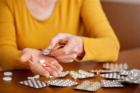 건강에 해로운 중년 노인 알 약을 들고 사용 하기 전에 정제를 풀다 많은 의약품 포장으로 가정용 주방 테이블에 앉아있는 노인을 닫습니다 고온 개념 다른 약을 먹다에 대한