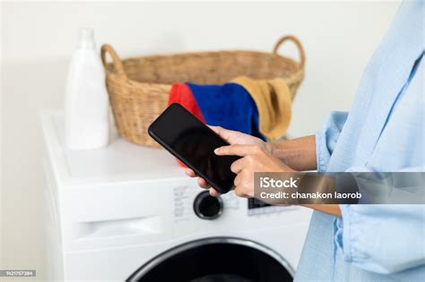클로즈업 주부 손은 응용 프로그램과 함께 휴대 전화를 사용하여 스마트 세탁기를 작동합니다 기술 스마트 폰으로 제어되는 옷을 청소하는 여성 가사 집안일에 대한 스톡 사진 및