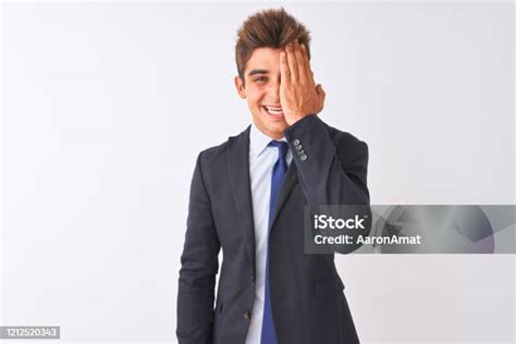 한 눈을 손으로 덮고 얼굴에 자신감 있는 미소와 깜짝 감정을 감싸고 있는 고립된 흰색 배경 위에 서 있는 젊은 잘생긴 사업가 가리기에 대한 스톡 사진 및 기타 이미지