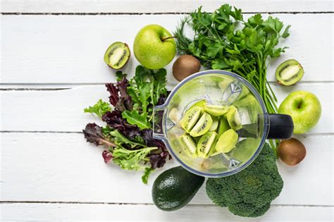 사과 키위 아보카도 양상추 브로콜리 딜 파슬리로 만든 건강한 녹색 스무디를 위한 재료로 흰색 나무 테이블에 있는 믹서기 유리