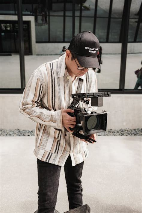 구름 남자 삼각대 서 있는 수직 쐈어 자켓 잡고 있는 촬영하는 카메라 캡 모자 흐린에 관한 무료 스톡 사진