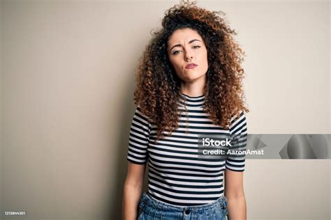 곱슬 머리와 피어싱 얼굴에 심각한 표정캐주얼 줄무늬 티셔츠를 입고 젊은 아름다운 여자 카메라를 보는 간단하고 자연스러운 T 셔츠에 대한 스톡 사진 및 기타 이미지 Istock