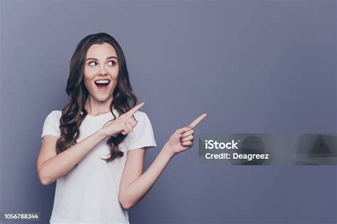 아름 다운 사랑 스러운 사랑 스러운 세련 된 명랑 기쁘게 곱슬 머리 여자 캐주얼 화이트에의 T셔츠 옆 두 손으로 가리키는 입을