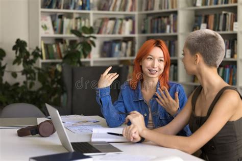 Excited Female Student Talk To Groupmate At Campus Library Desk Stock