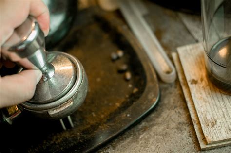 바리스타는 수동 프레스 분쇄 커피를 조작하기 위해 Portafilter와 금속 탬퍼를 손으로 잡습니다 갈색에 대한 스톡 사진 및