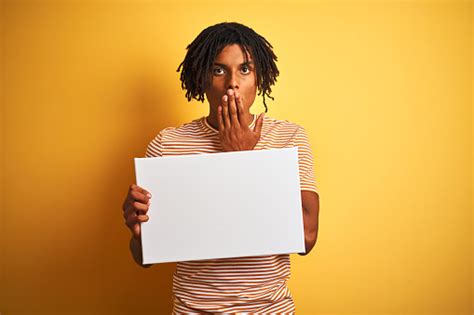 고립 된 노란색 배경 커버 입에 배너를 들고 공포를 가진 아프로 미국 남자는 실수 두려움의 표현 침묵 비밀 개념에 대한 수치심으로 충격을 받았다 가리기에 대한 스톡 사진 및